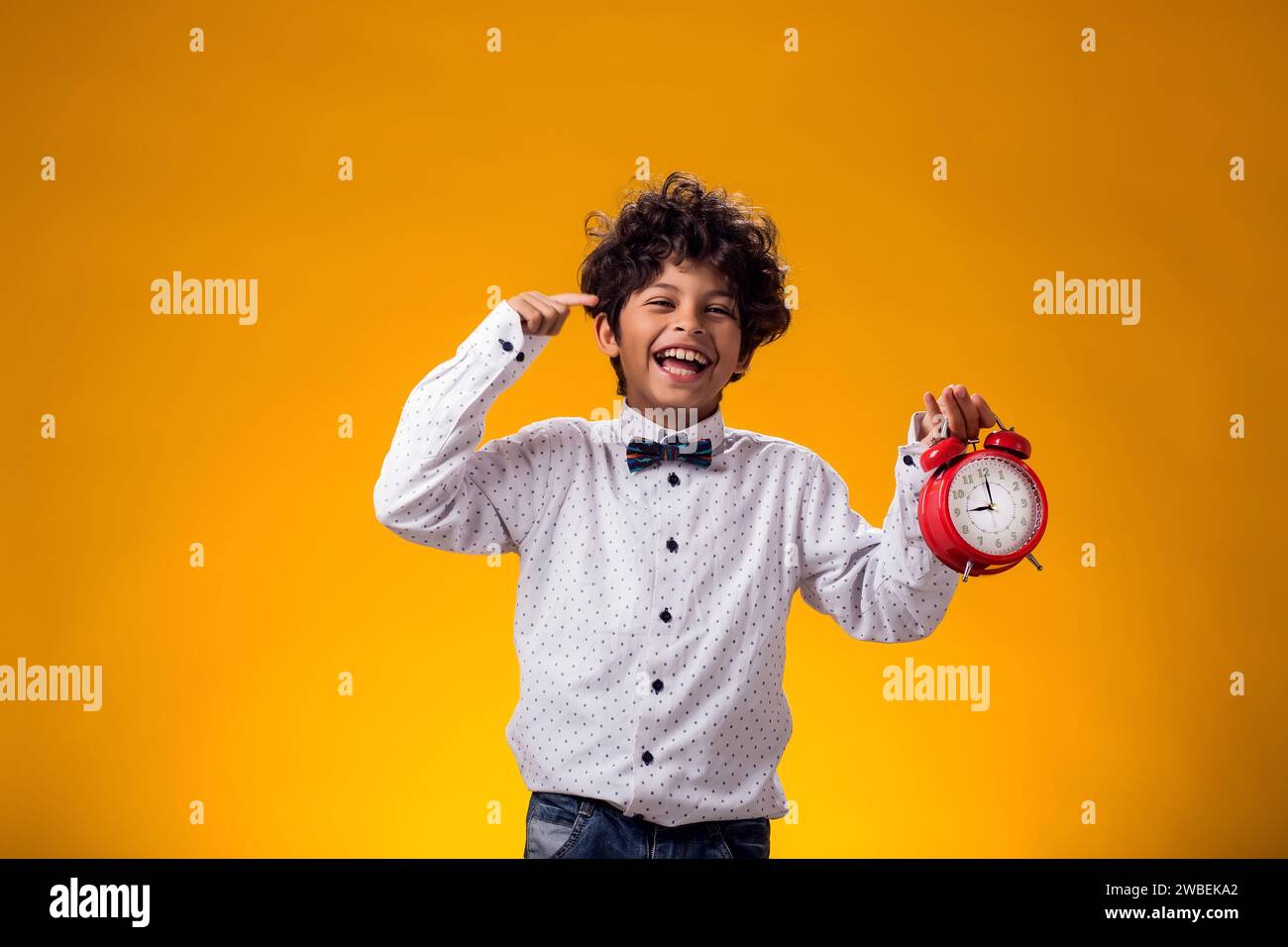 Portrait of child boy holding alarm clock over yellow background. Time ...