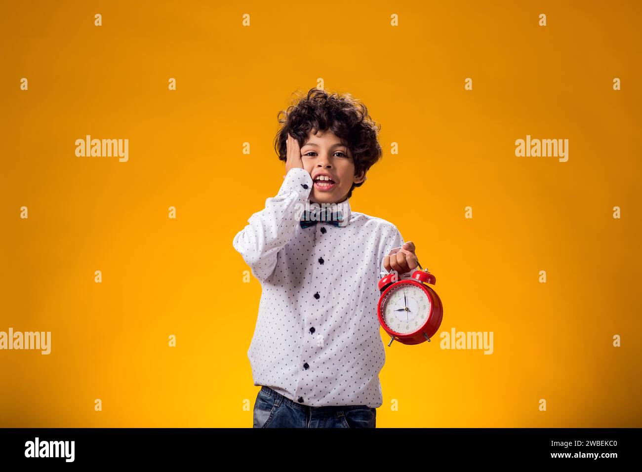 Portrait of surprised child boy holding alarm clock over yellow ...