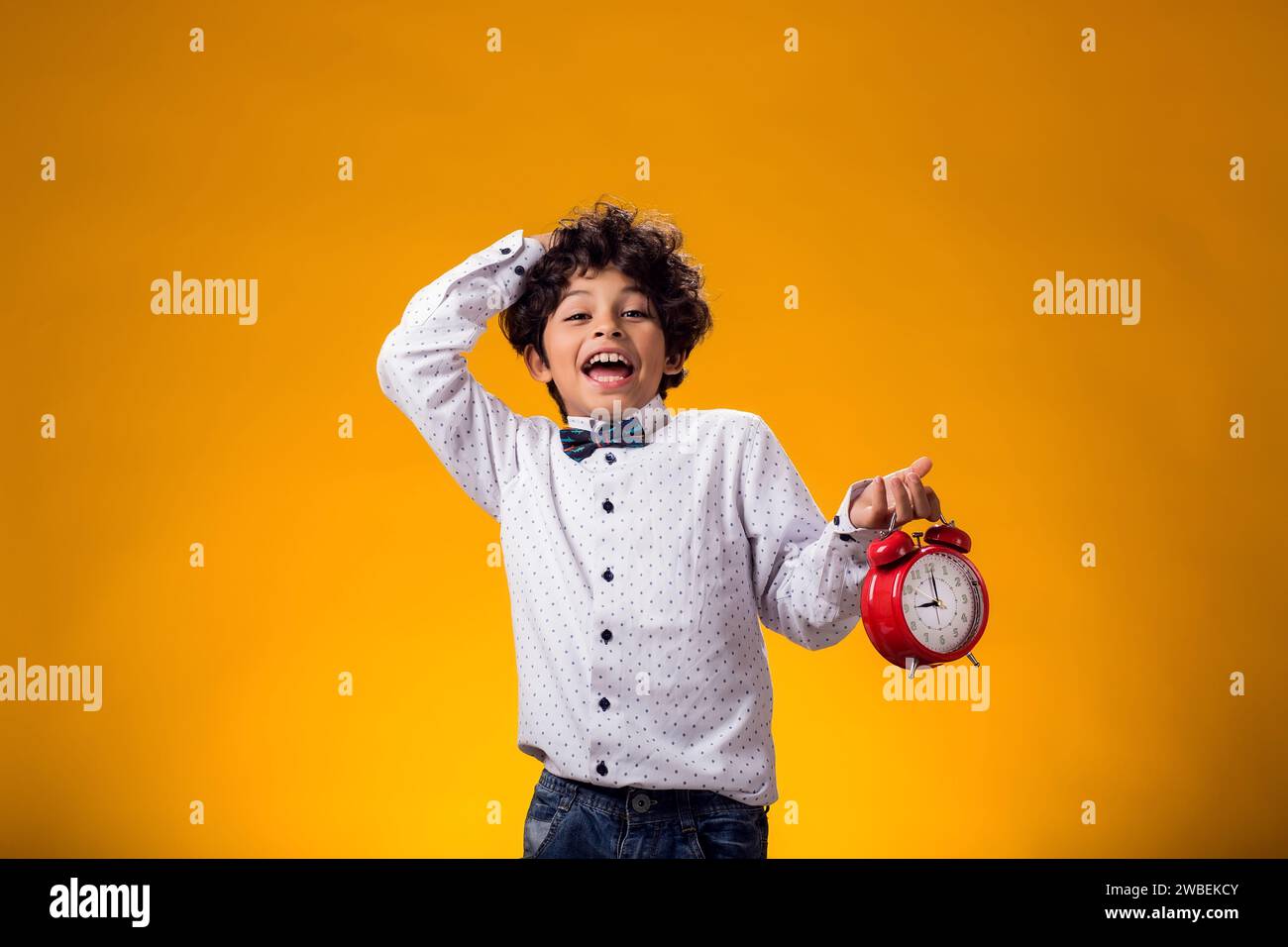 Portrait of surprised child boy holding alarm clock over yellow ...