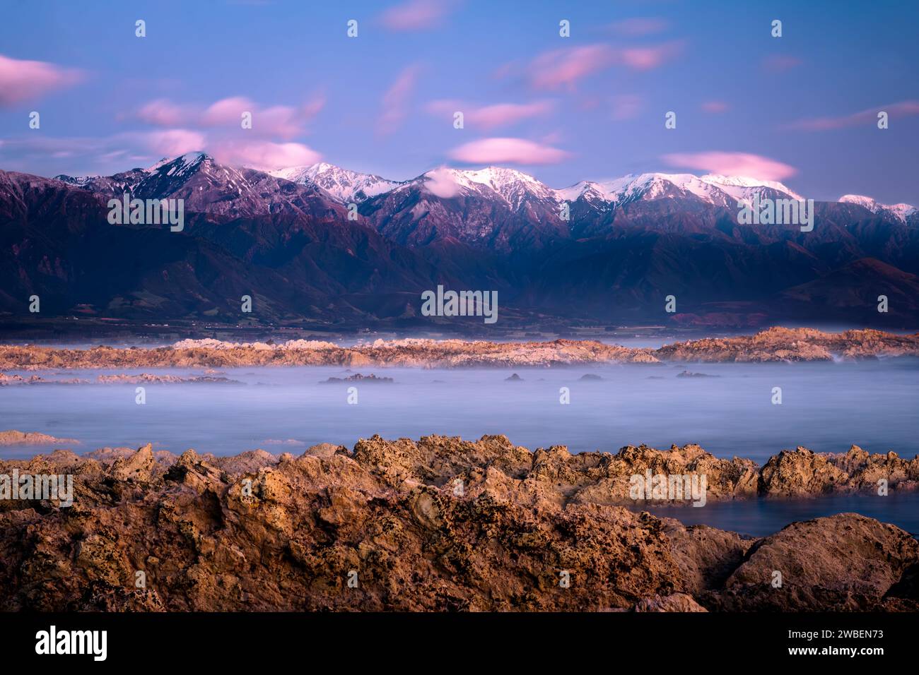 Coastal scene at dawn of bay with foreground rocks, sea and distant ...
