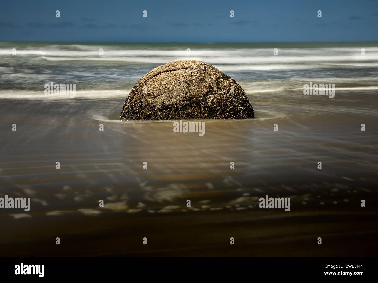 Fine art scene of single round boulder, half embedded in beach, with ...