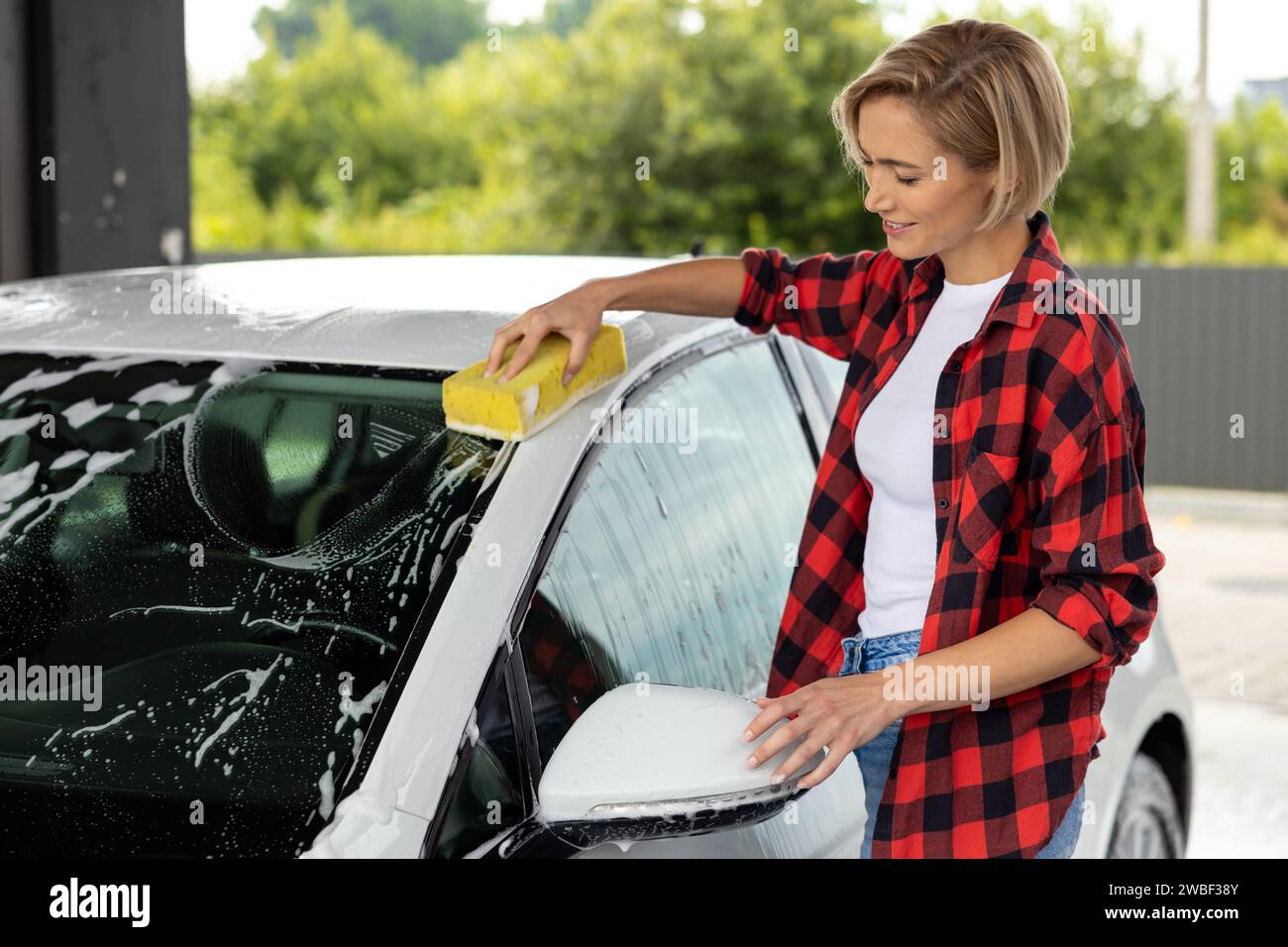 Blonde young woman washing car windscreen and looking involved Stock ...