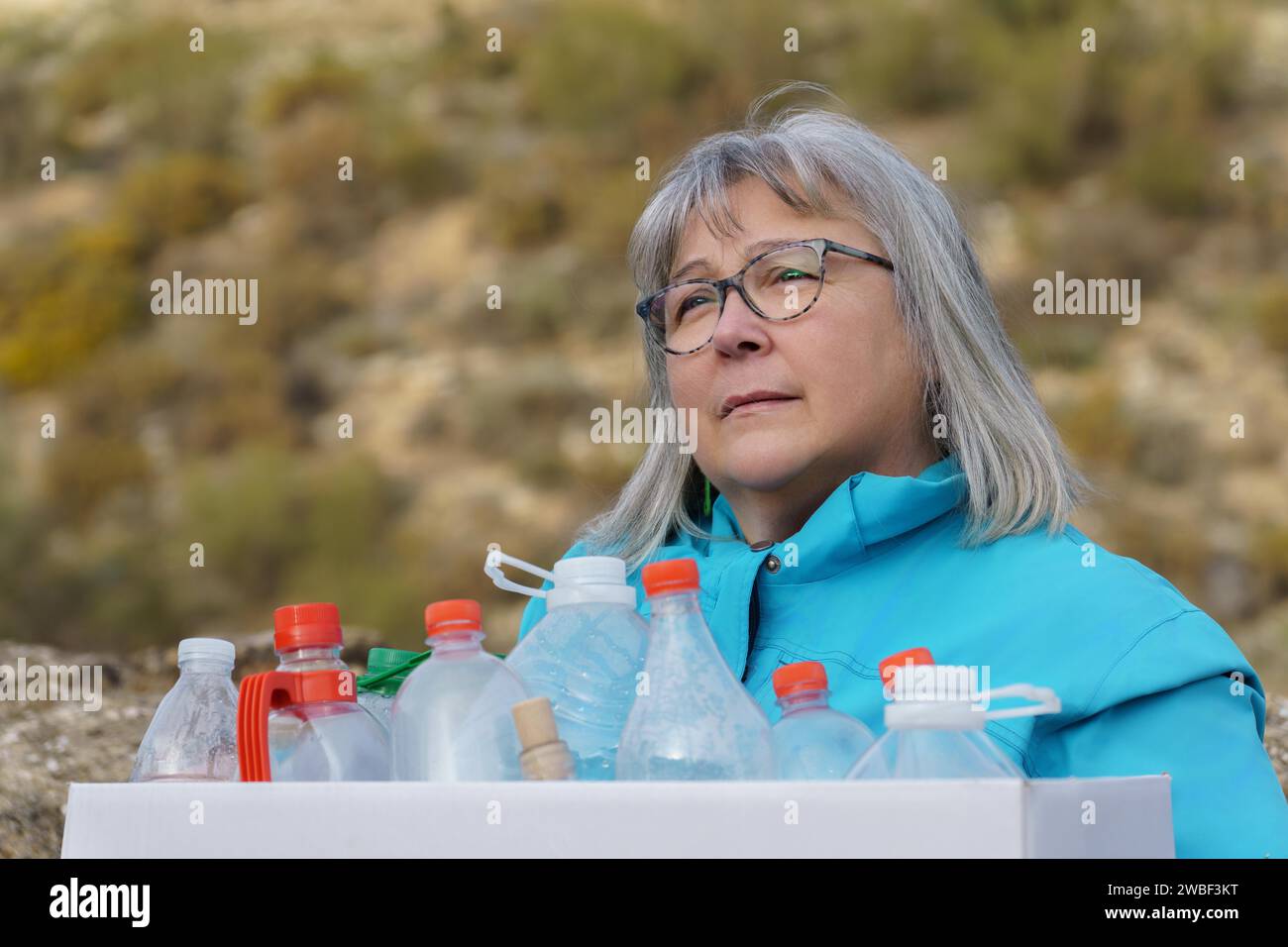 Older white-haired woman holding a cardboard box full of empty plastic ...