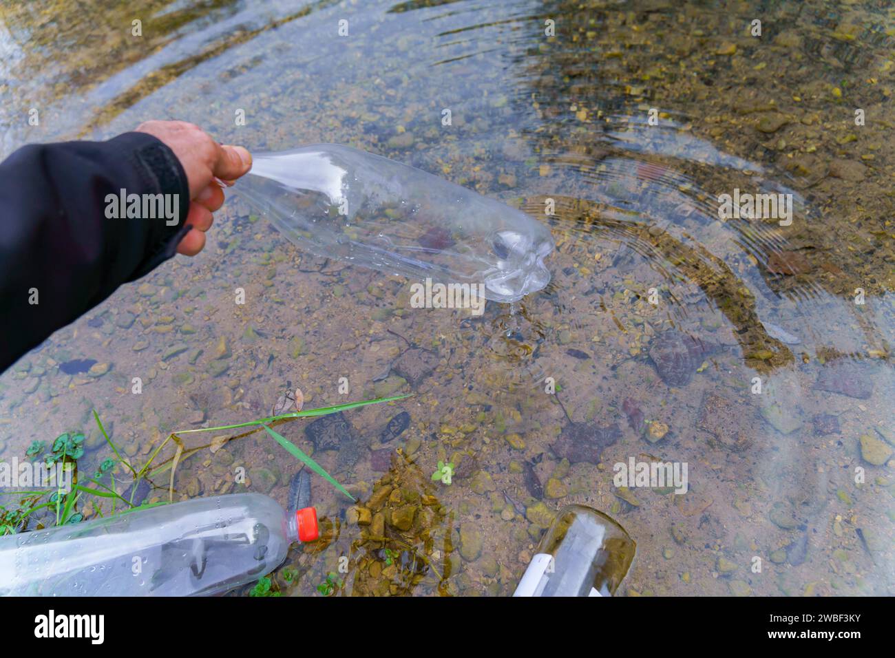 Man collecting plastic bottles on the shore of a river, environmental ...