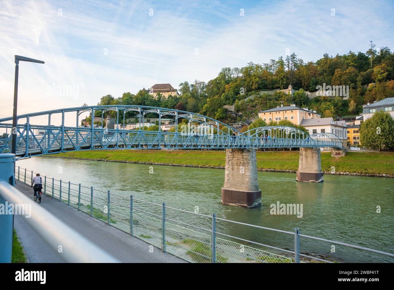 A long blue bridge over a river with green banks and blue sky ...