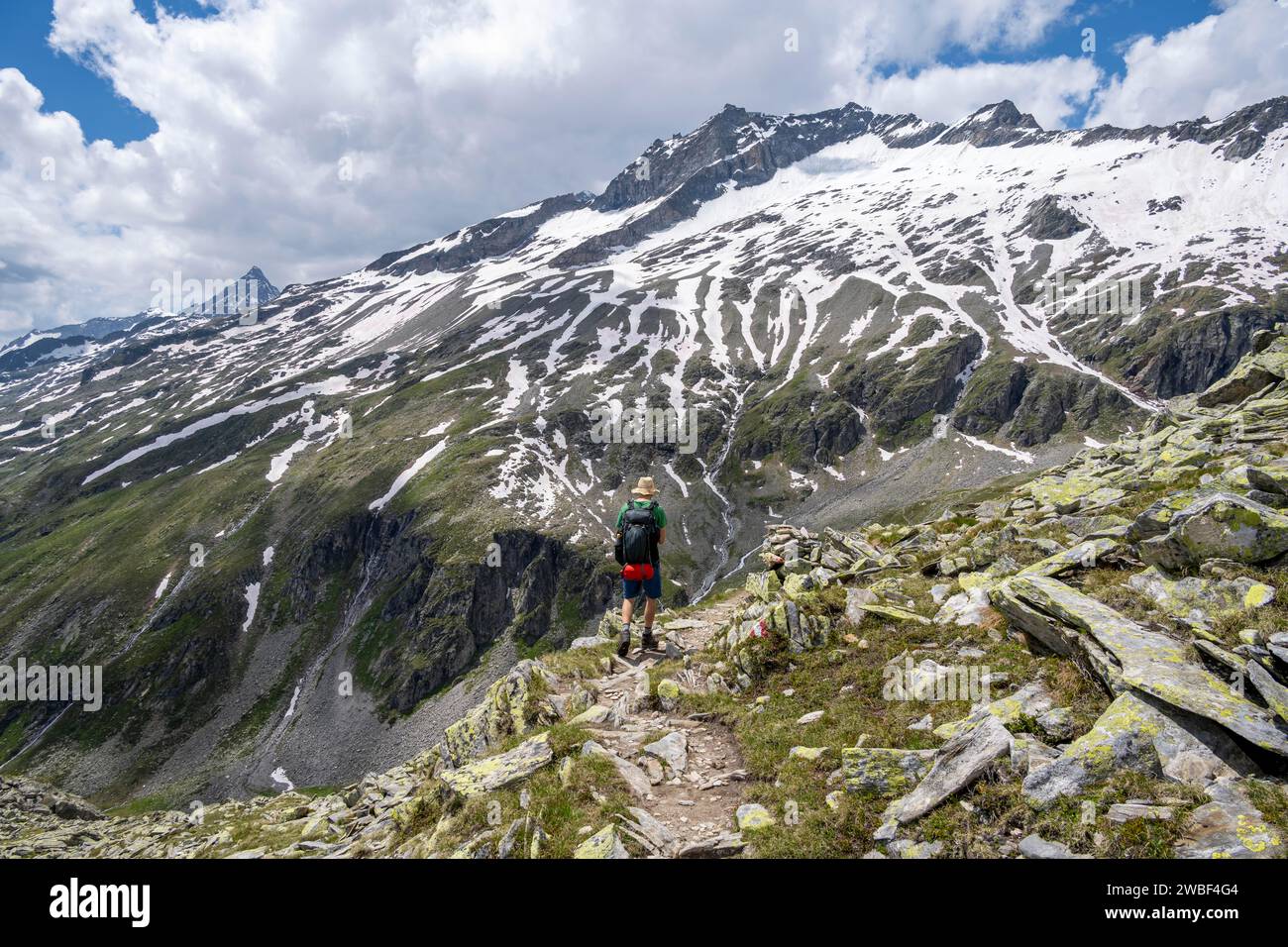 Mountaineer on rocky hiking trail, Berliner Hoehenweg, mountain landscape with snow-covered peak ...
