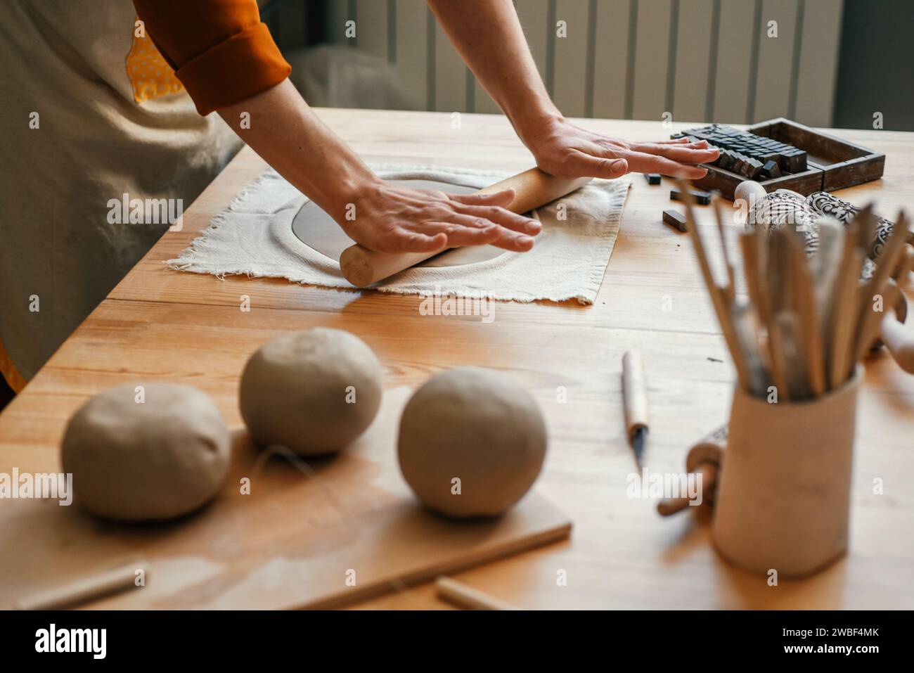Artisan woman in lighted pottery studio, rolling clay for modelling ...