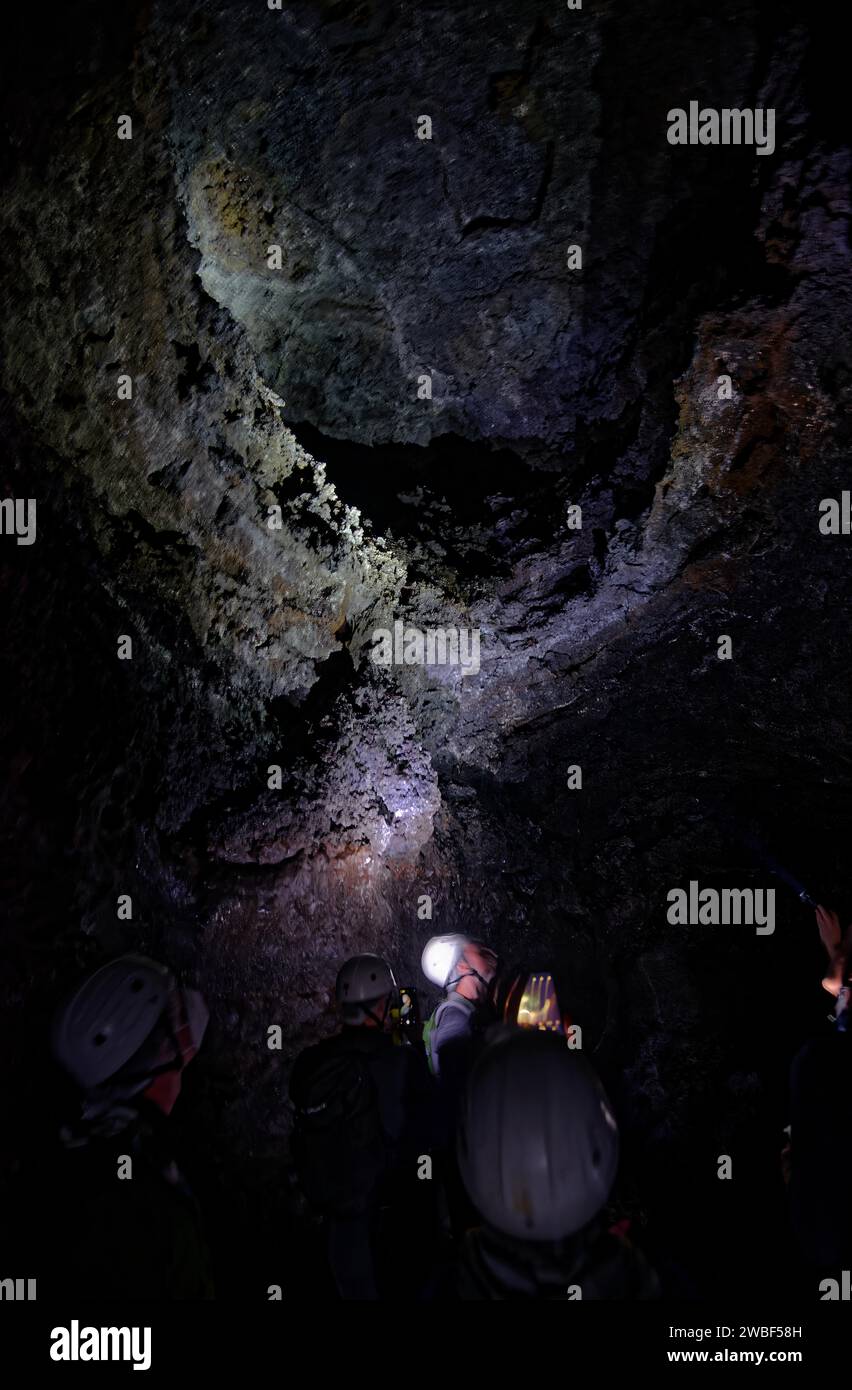 Cave explorers in the lava tunnel Gruta das Torres with helmets looking ...