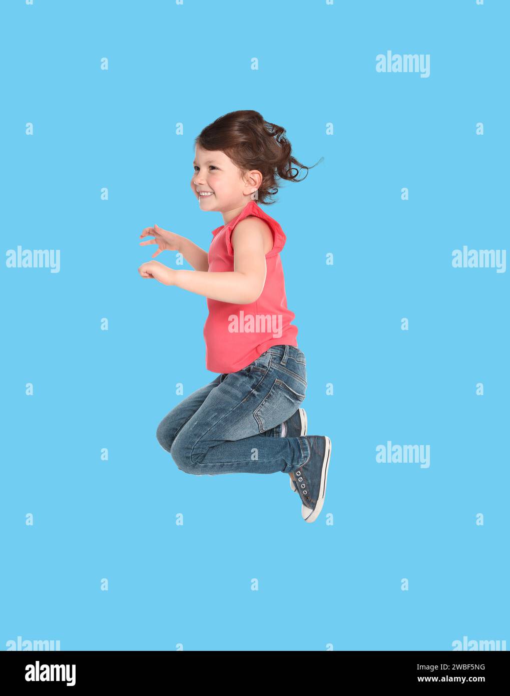 Happy cute girl jumping on light blue background Stock Photo - Alamy
