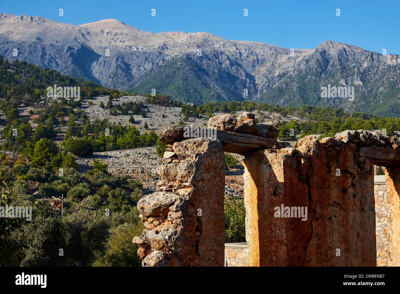 Remains of an ancient wall against a mountain backdrop under a blue sky ...