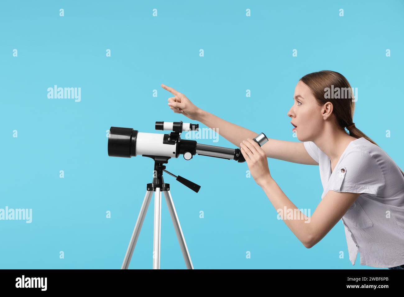 Surprised astronomer with telescope pointing at something on light blue ...