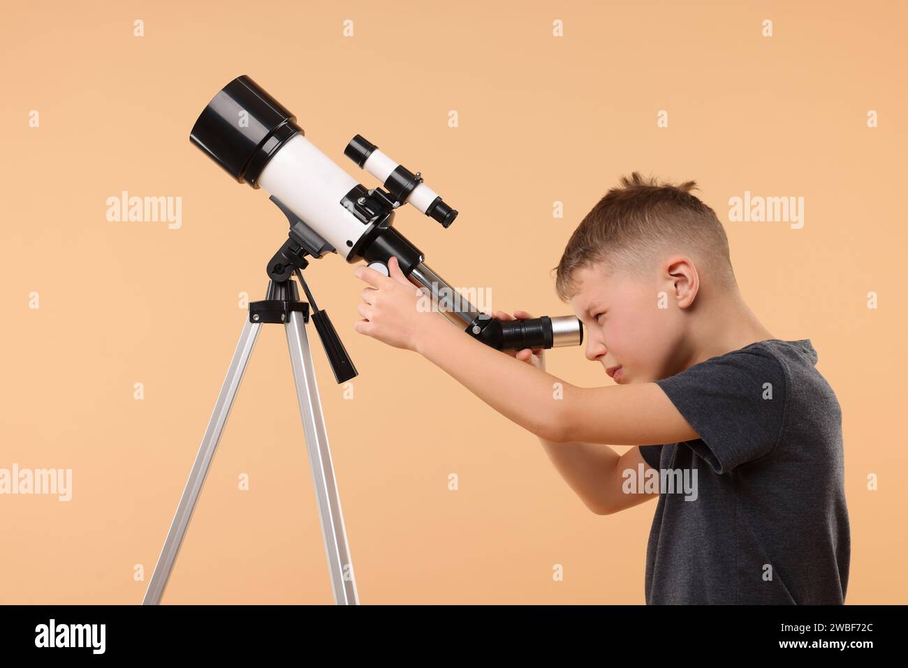 Little boy looking at stars through telescope on beige background Stock ...