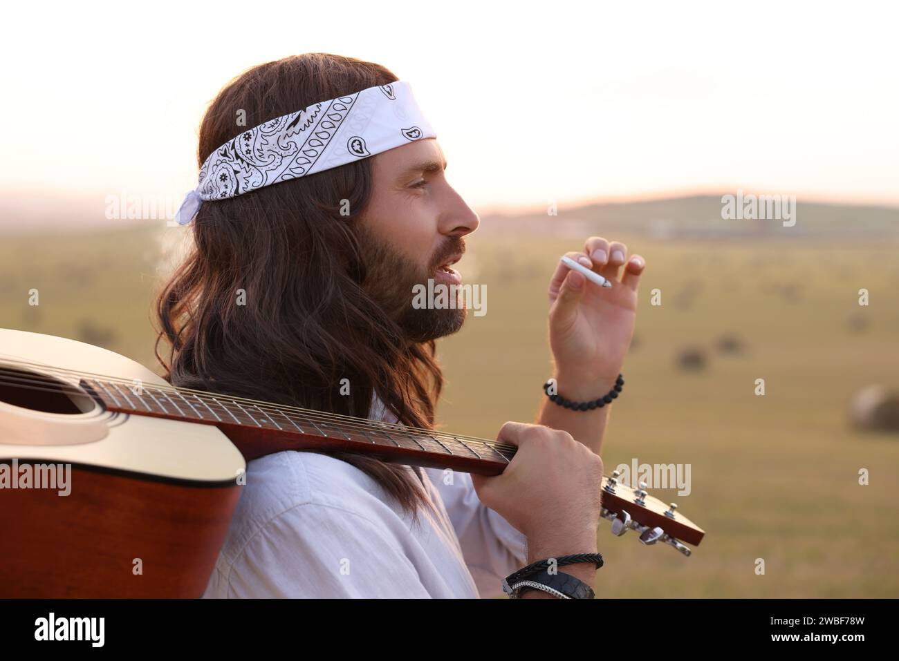 Stylish hippie man with guitar smoking joint in field Stock Photo - Alamy
