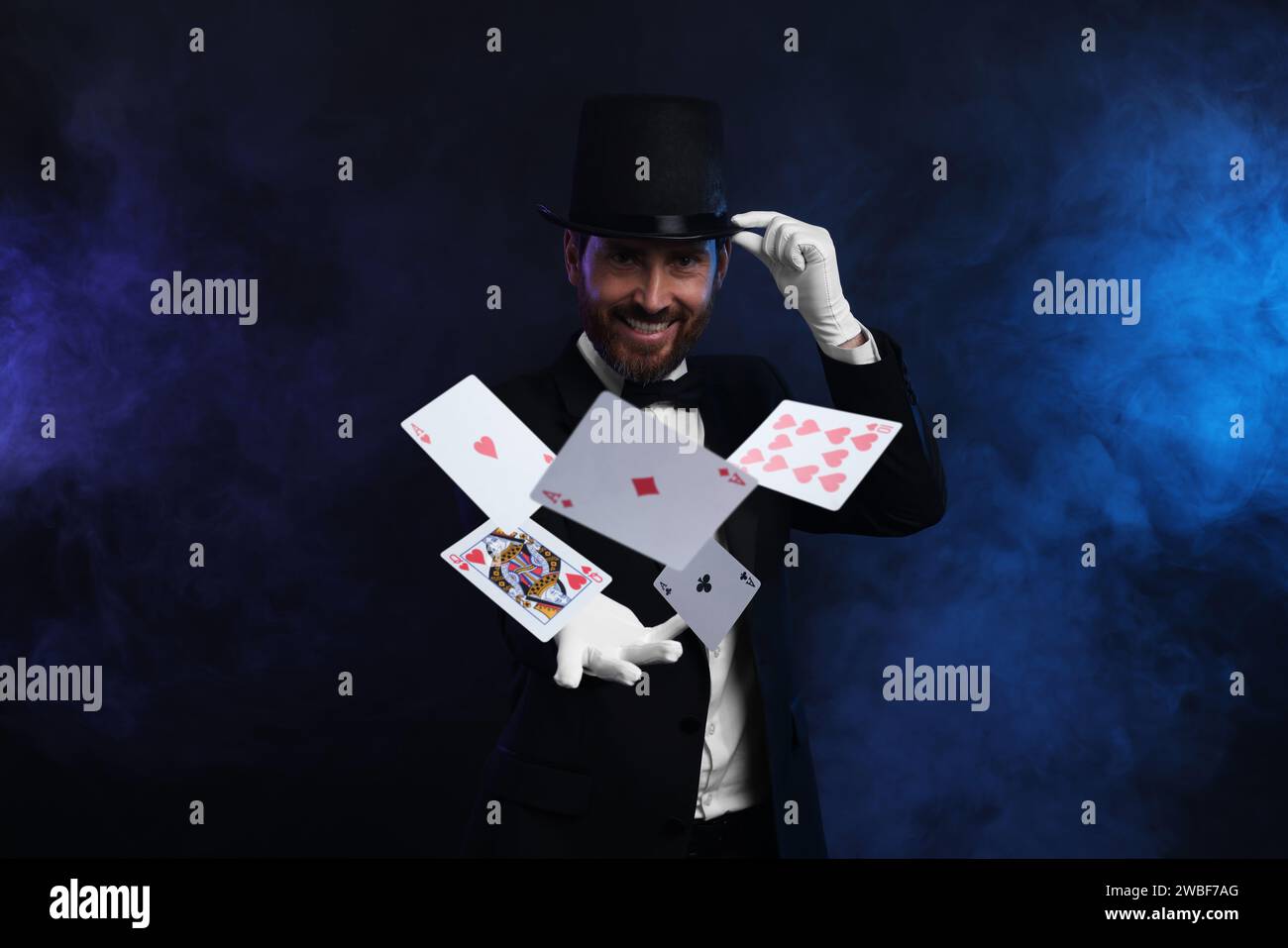 Smiling magician showing trick with cards on dark blue background Stock ...