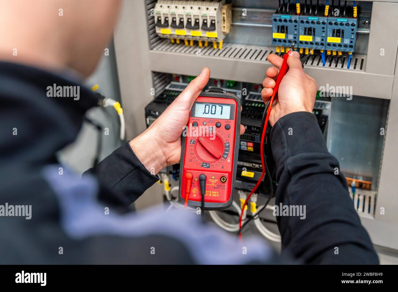 Worker measuring and repairing an electrical system panel in a factory ...