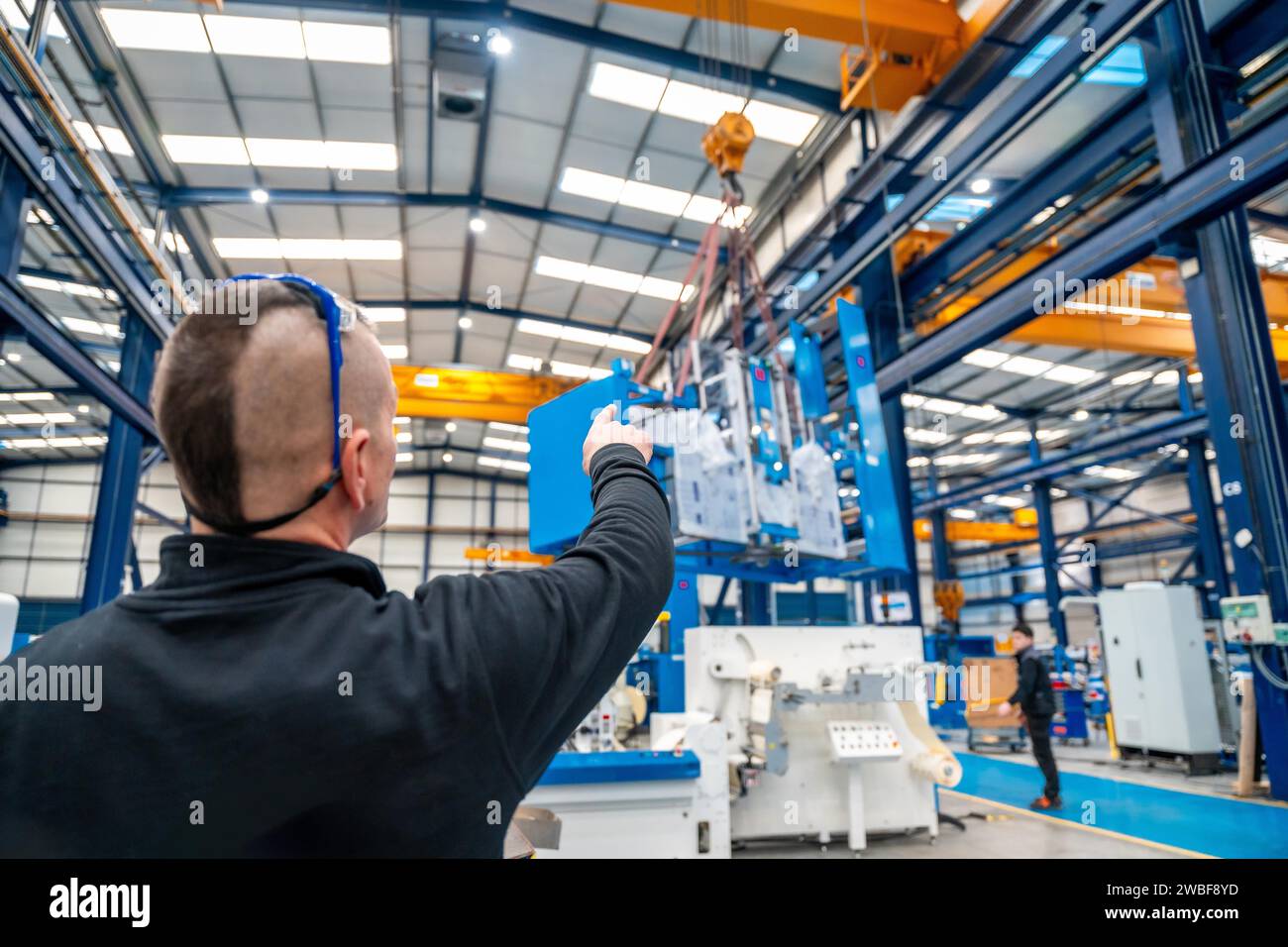 Rear view of a worker directing the maneuvers of an industrial crane ...