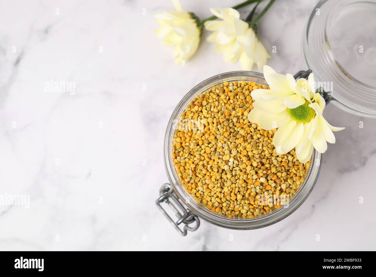 Fresh bee pollen granules in jar and flowers on light table, top view ...