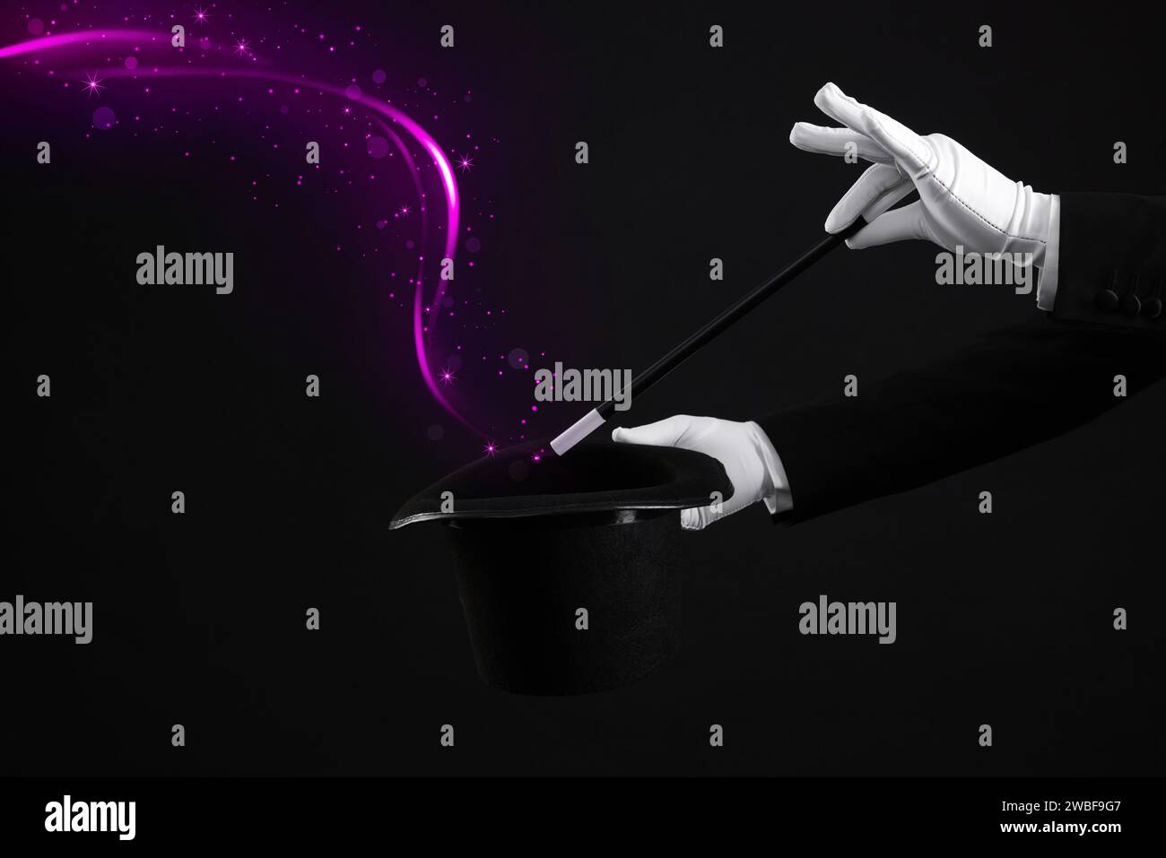 Magician showing trick with wand and top hat on black background ...