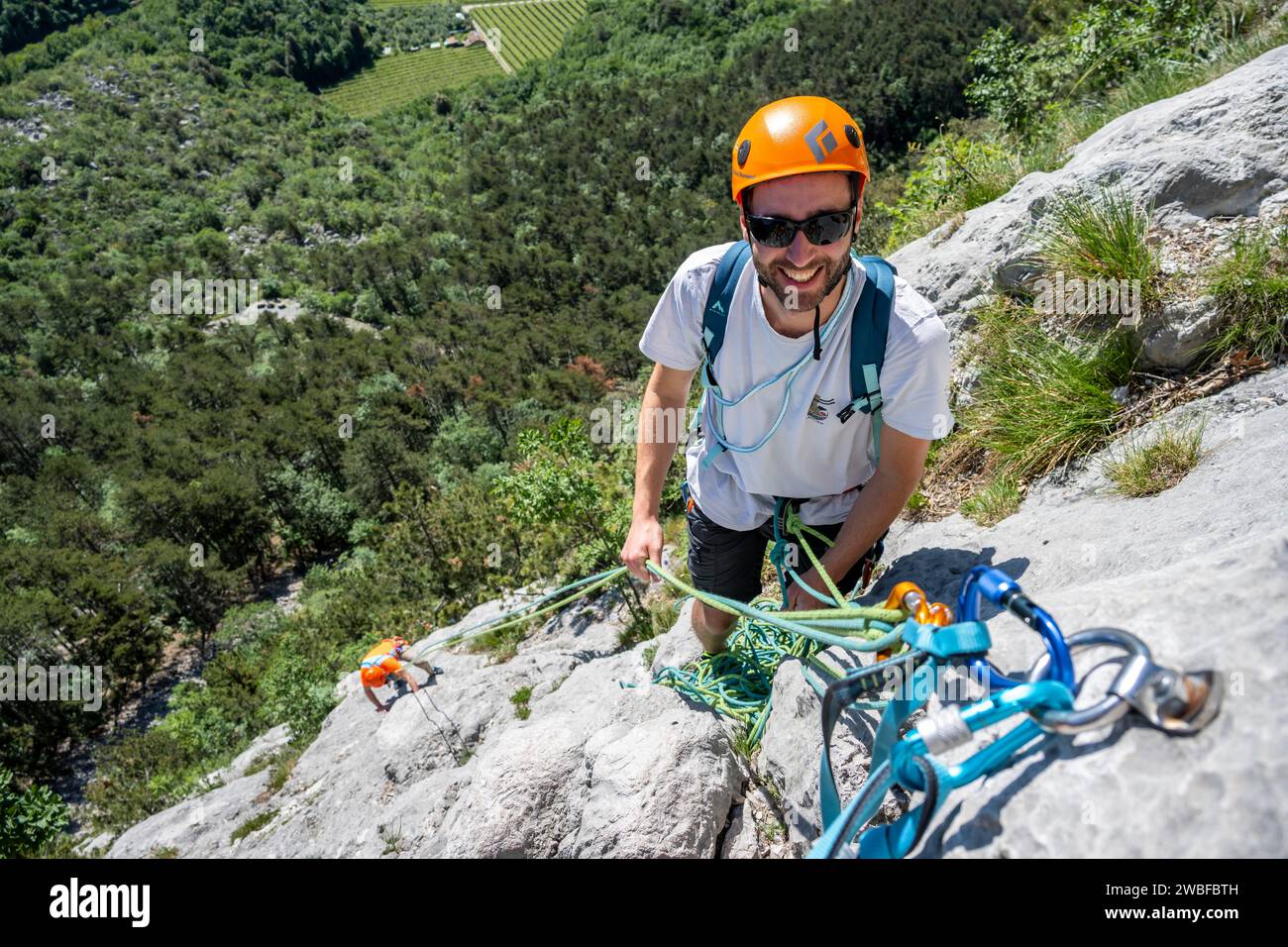 A smiling climber in a safety helmet secures himself to a rock with ...