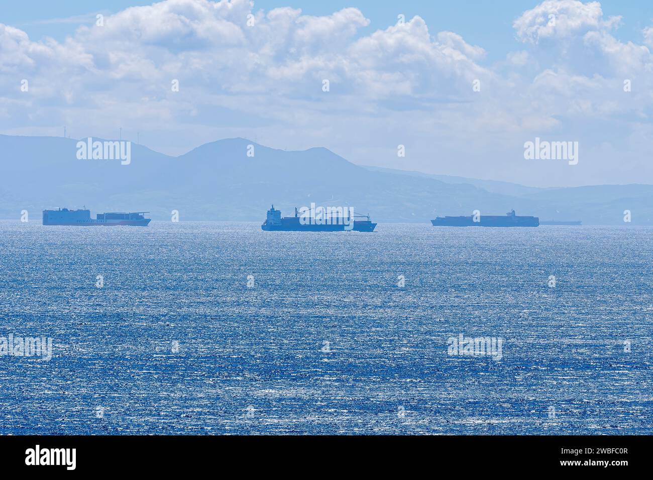 Three large cargo ships floating on a shimmering blue sea against a ...