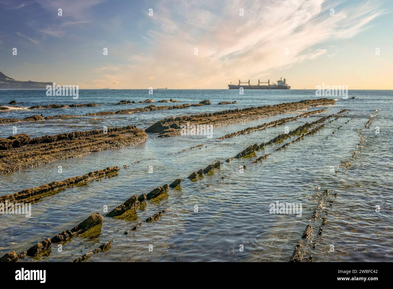 Calm coastal waters with visible rock formations leading to cargo ships ...