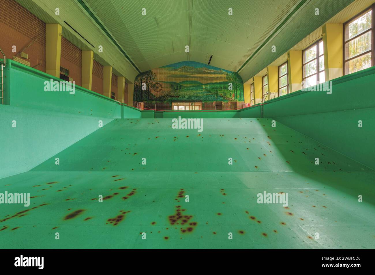 A dilapidated, empty swimming pool with rust stains on the floor ...
