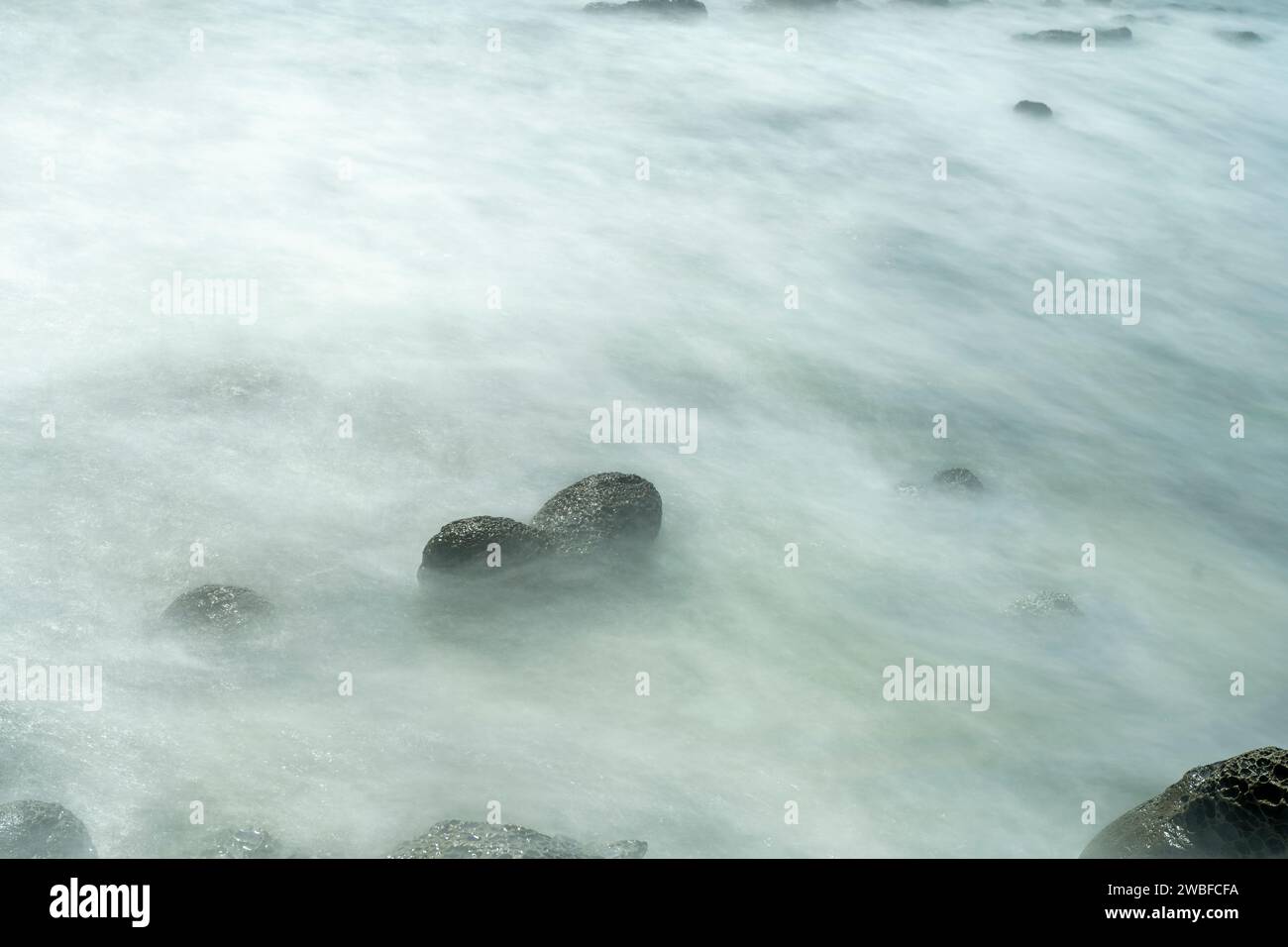 A long-exposure shot captures the serene motion of misty waves swirling ...