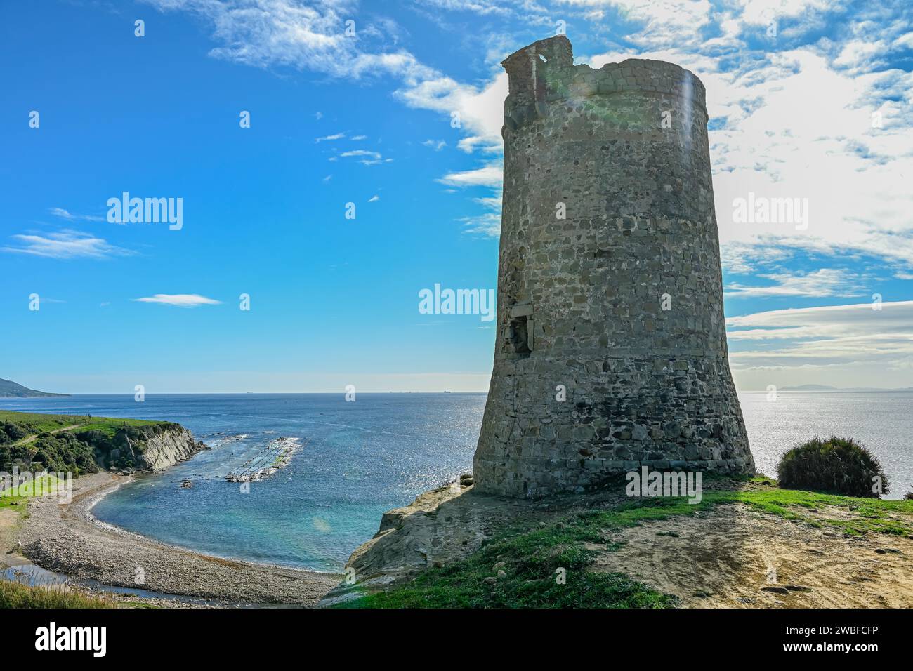 An ancient stone watchtower stands atop a cliff with lush greenery ...