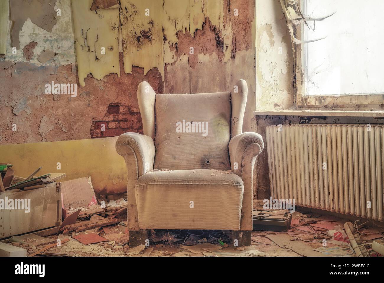 A worn armchair in front of a crumbling wall with falling wallpaper in ...