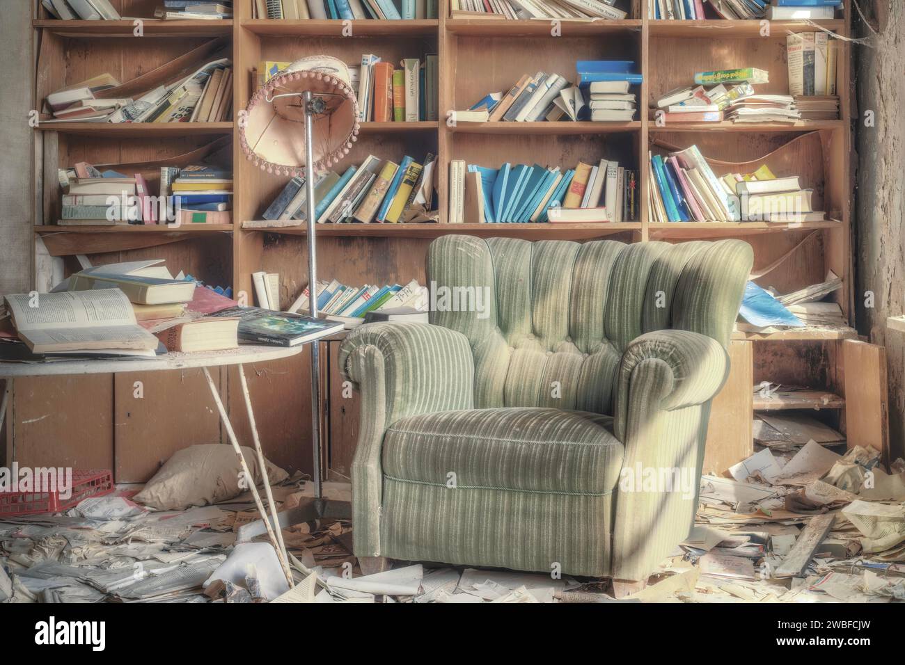 A lonely armchair in front of an overcrowded bookshelf in a decaying ...
