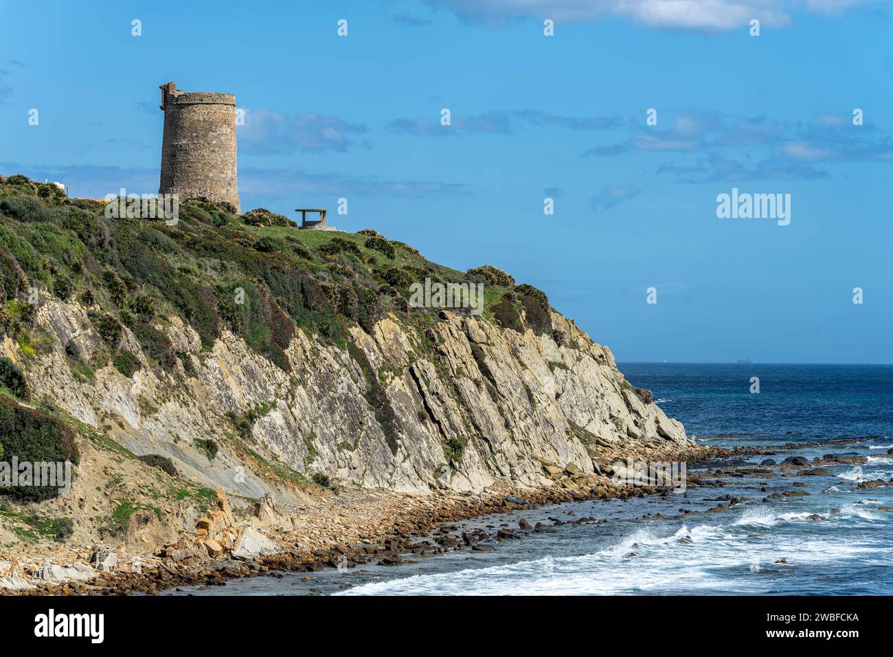 An ancient stone watchtower stands atop a cliff with lush greenery ...