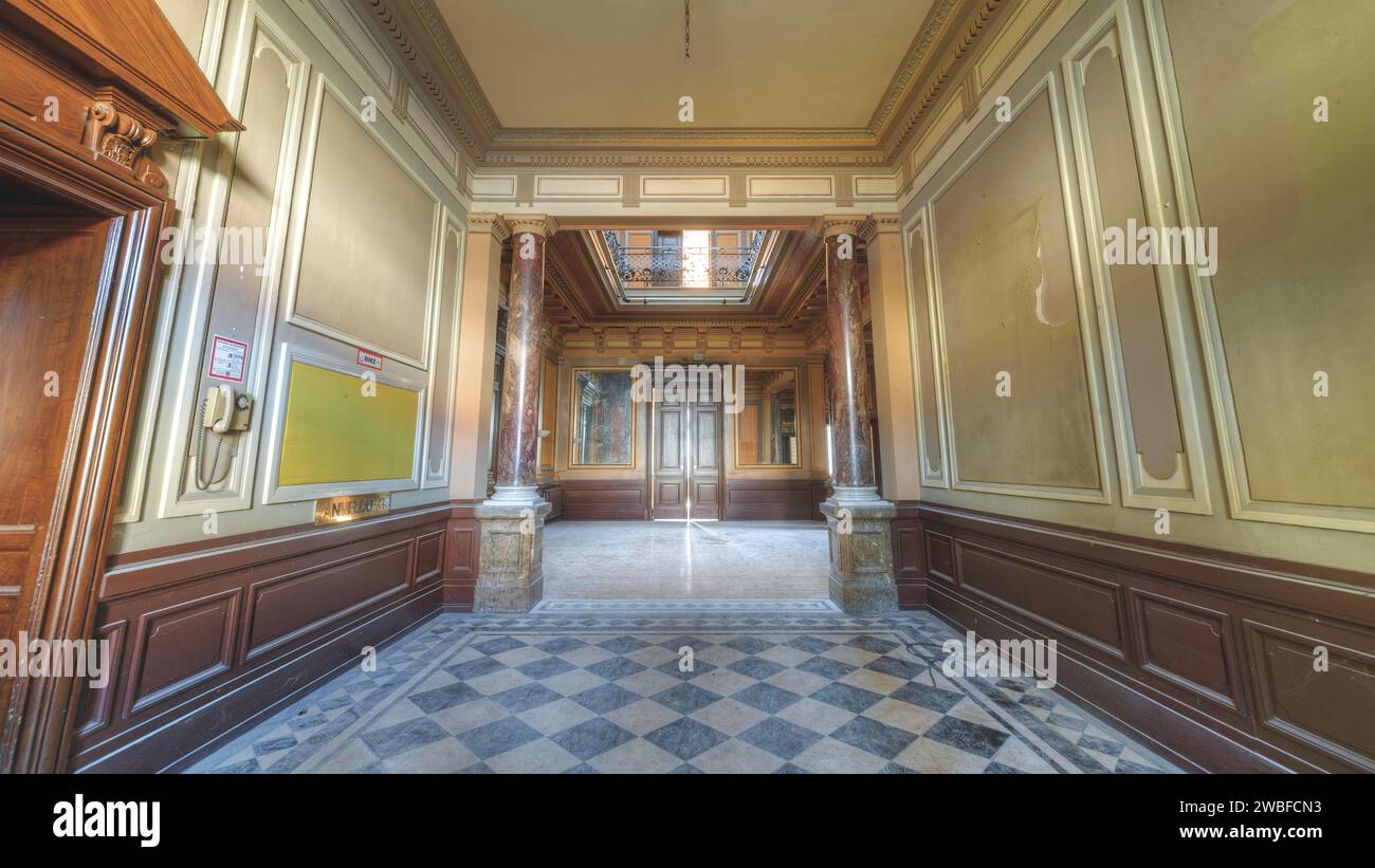 A hallway in a historic building with chequered floor tiles and pillar ...