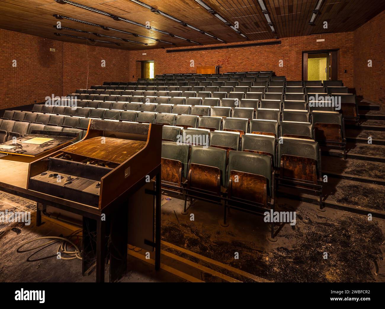 A dark lecture theatre with heavily worn seats and an abandoned lectern ...