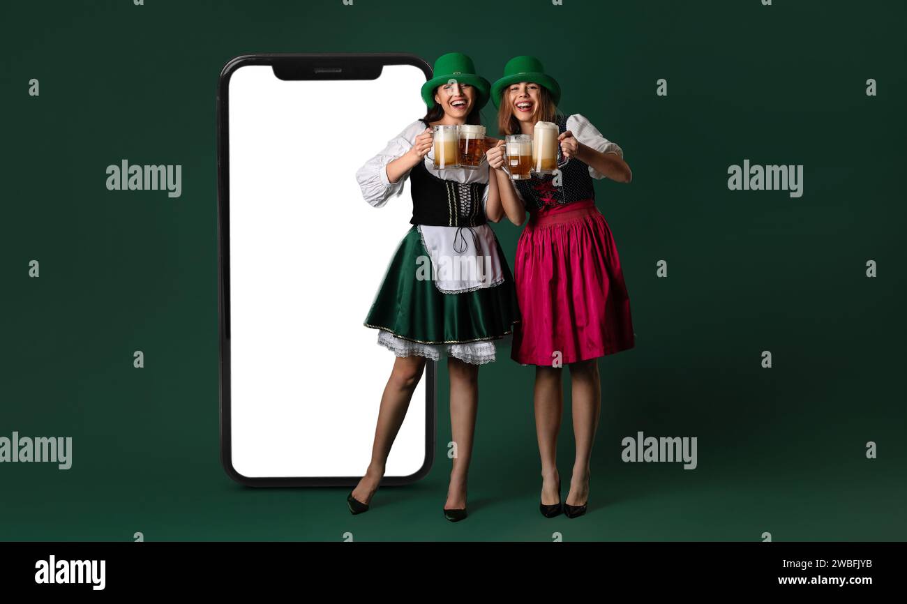Irish waitresses with beer and big smartphone on green background. St ...