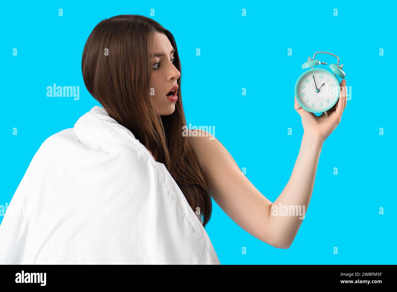 Upset young woman with alarm clock and soft blanket on blue background ...
