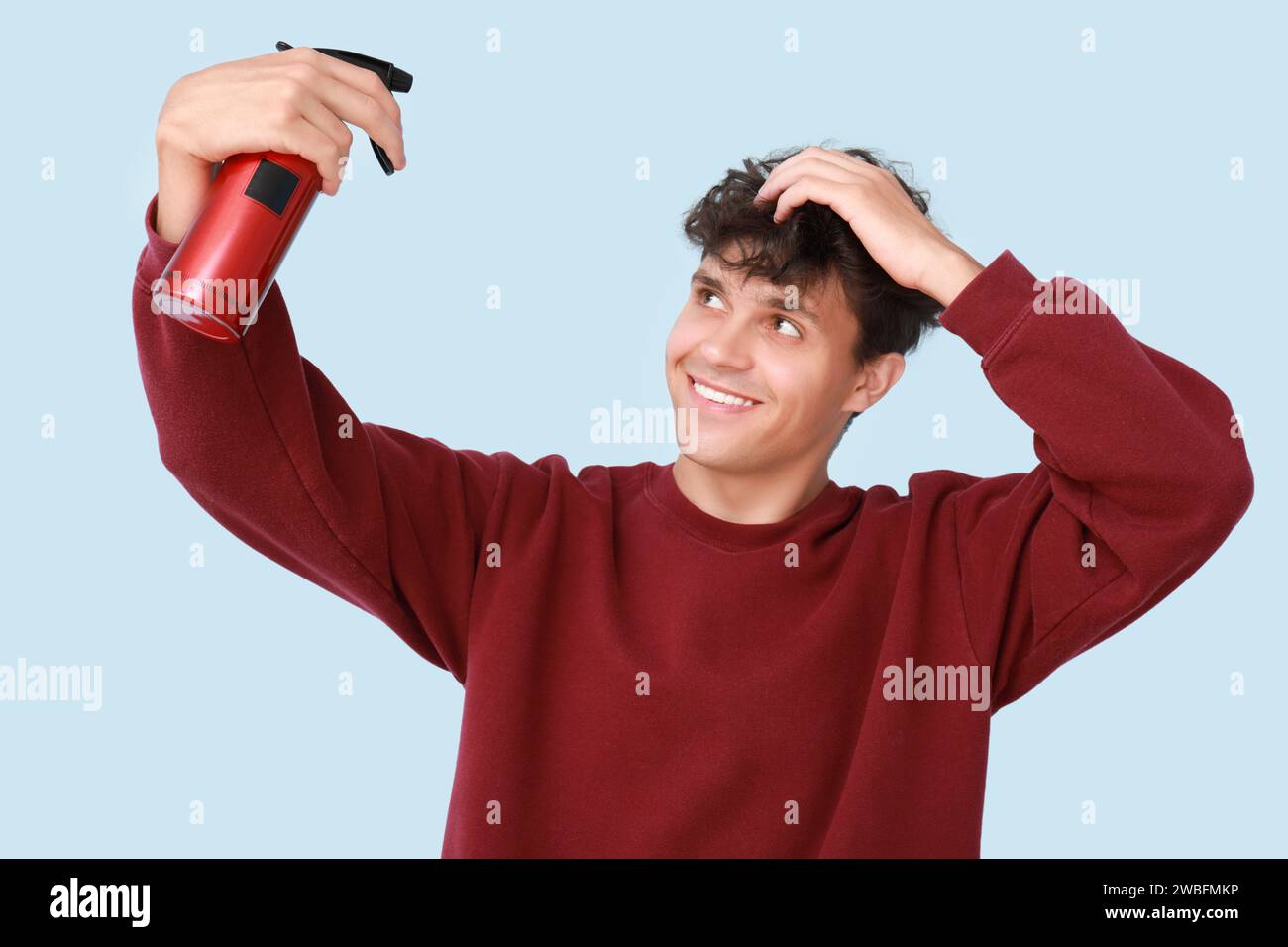 Handsome young man applying hair spray on his curly hair against blue ...
