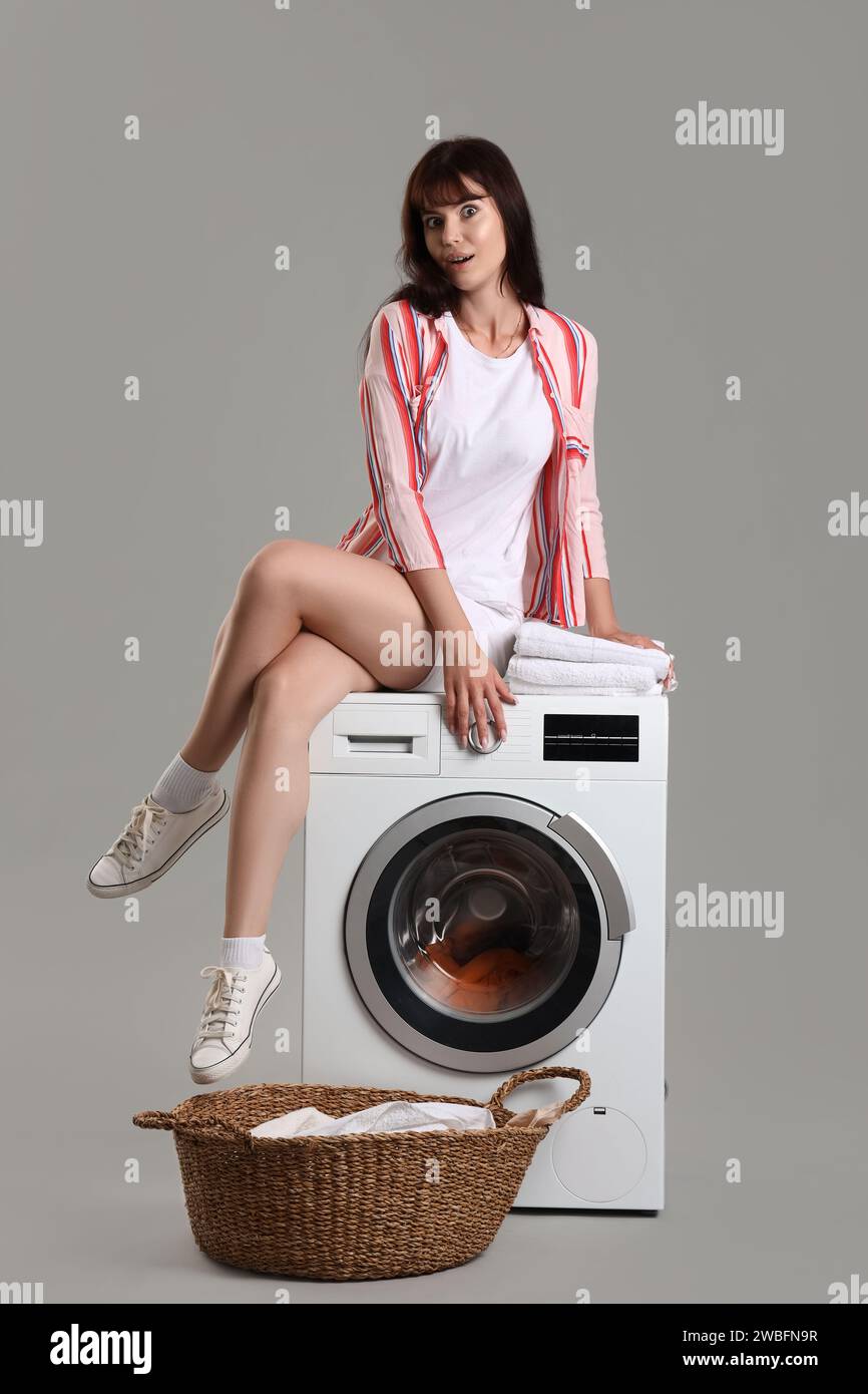 Young woman sitting on washing machine against grey background Stock ...