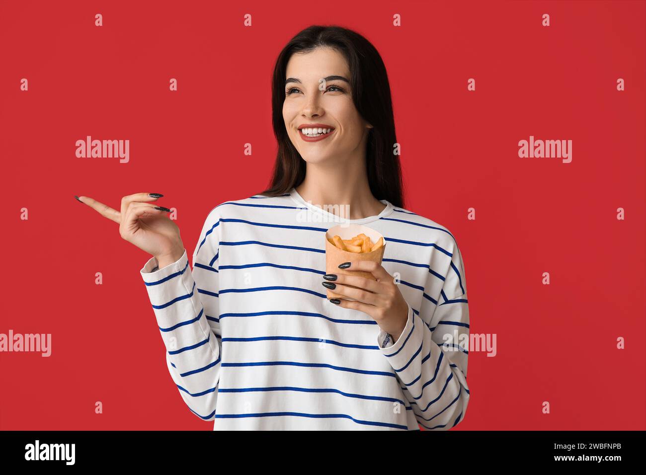 Beautiful young woman with french fries pointing at something on red ...