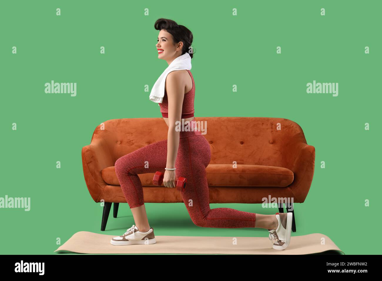 Sporty young pin-up woman with dumbbells training on green background ...