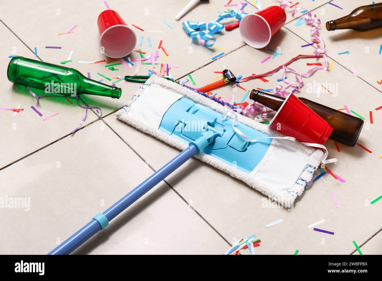 Mop with confetti, cups and bottles on tile floor after party, closeup ...