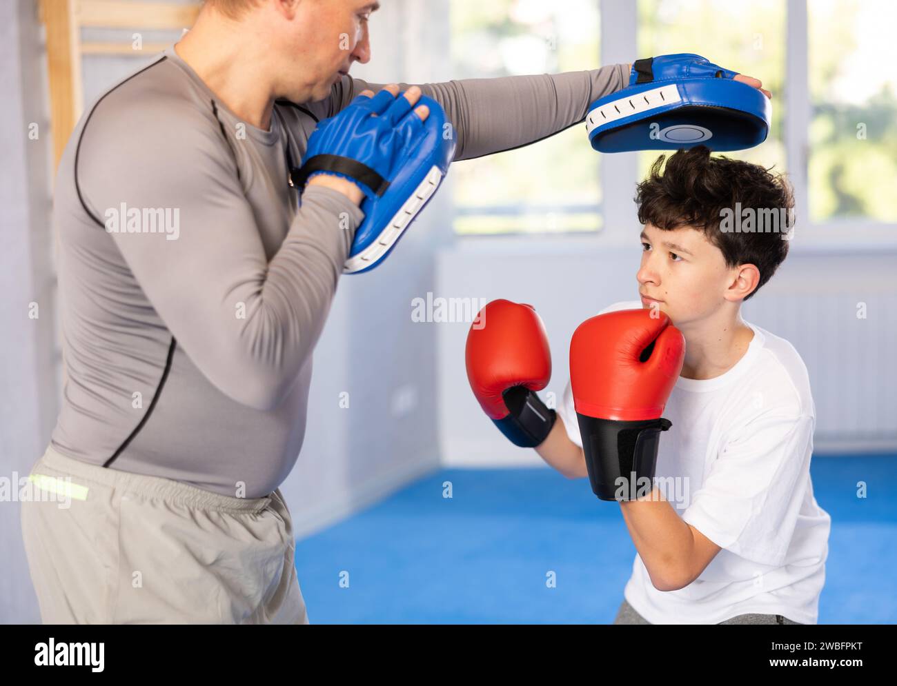 Teenage boy training boxing kicks on punch mitts held by instructor ...