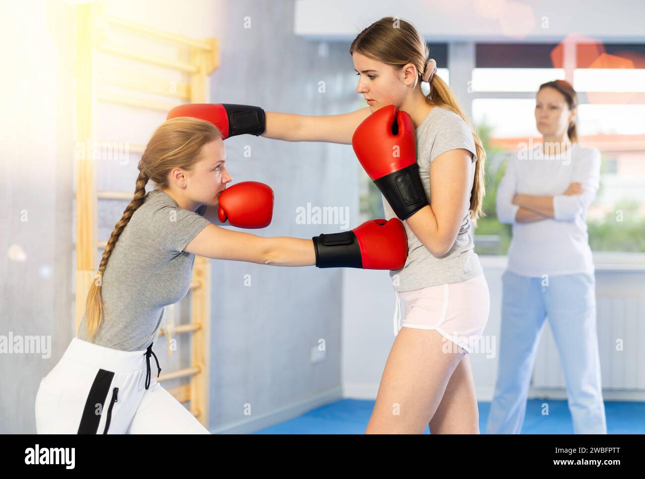 Teen girl in boxing gloves practicing punches in sparring during self ...