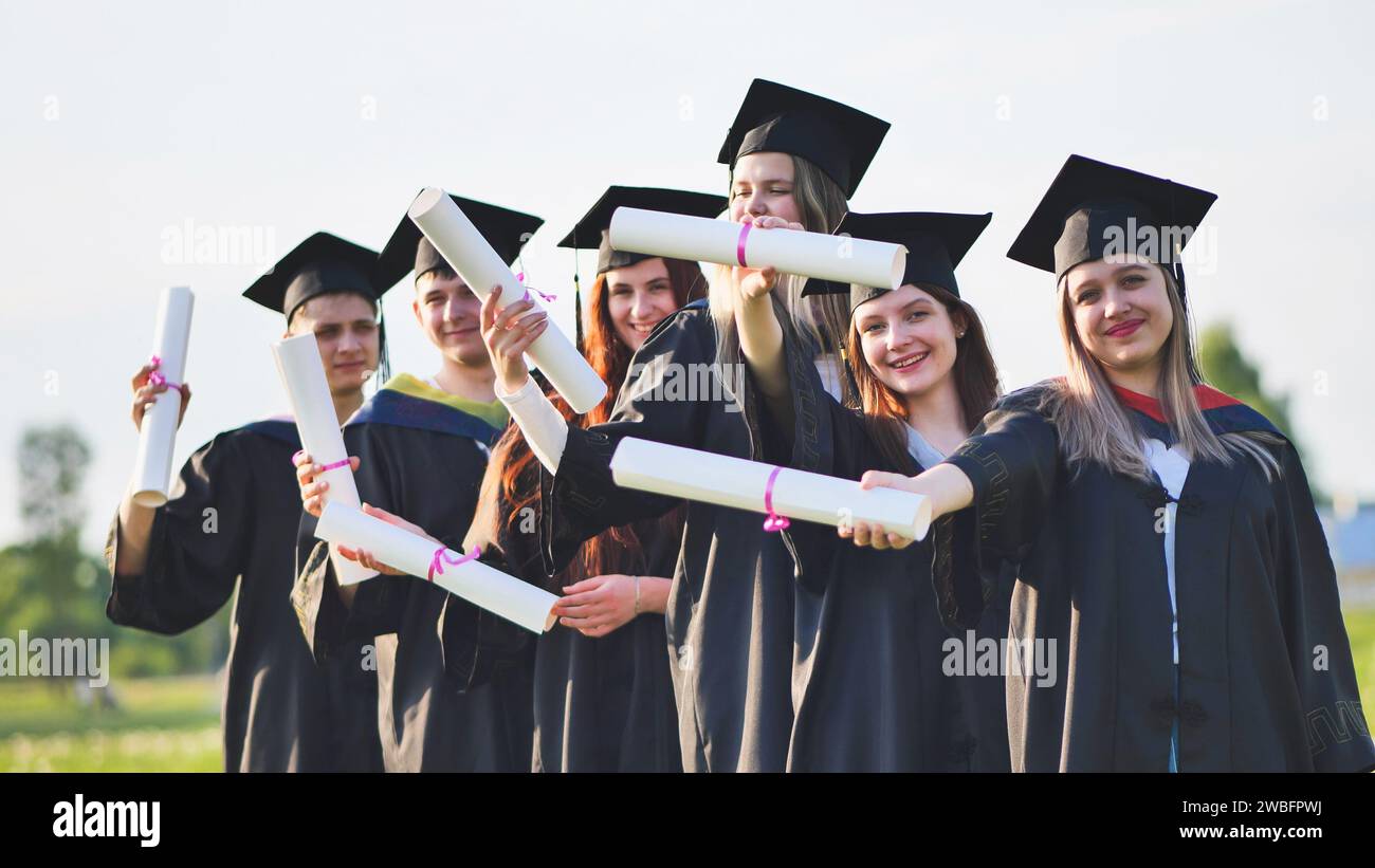 Cheerful graduates pose with raised diplomas on a sunny day Stock Photo ...
