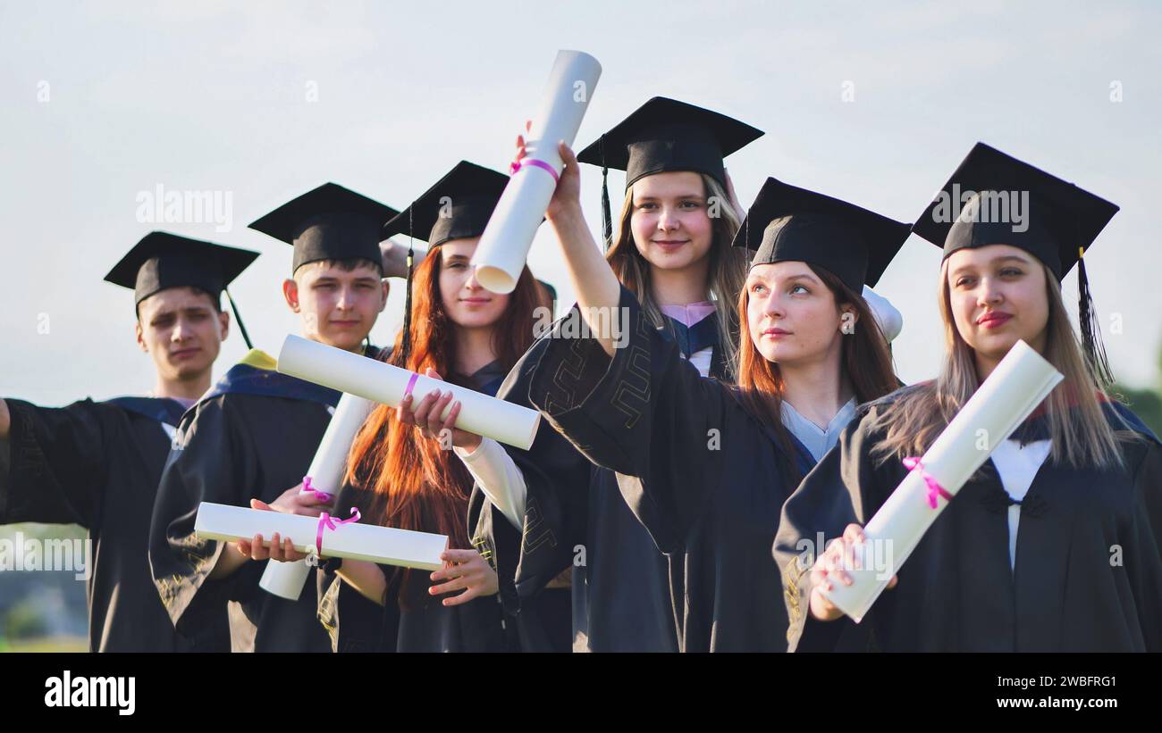 Cheerful graduates pose with raised diplomas on a sunny day Stock Photo ...