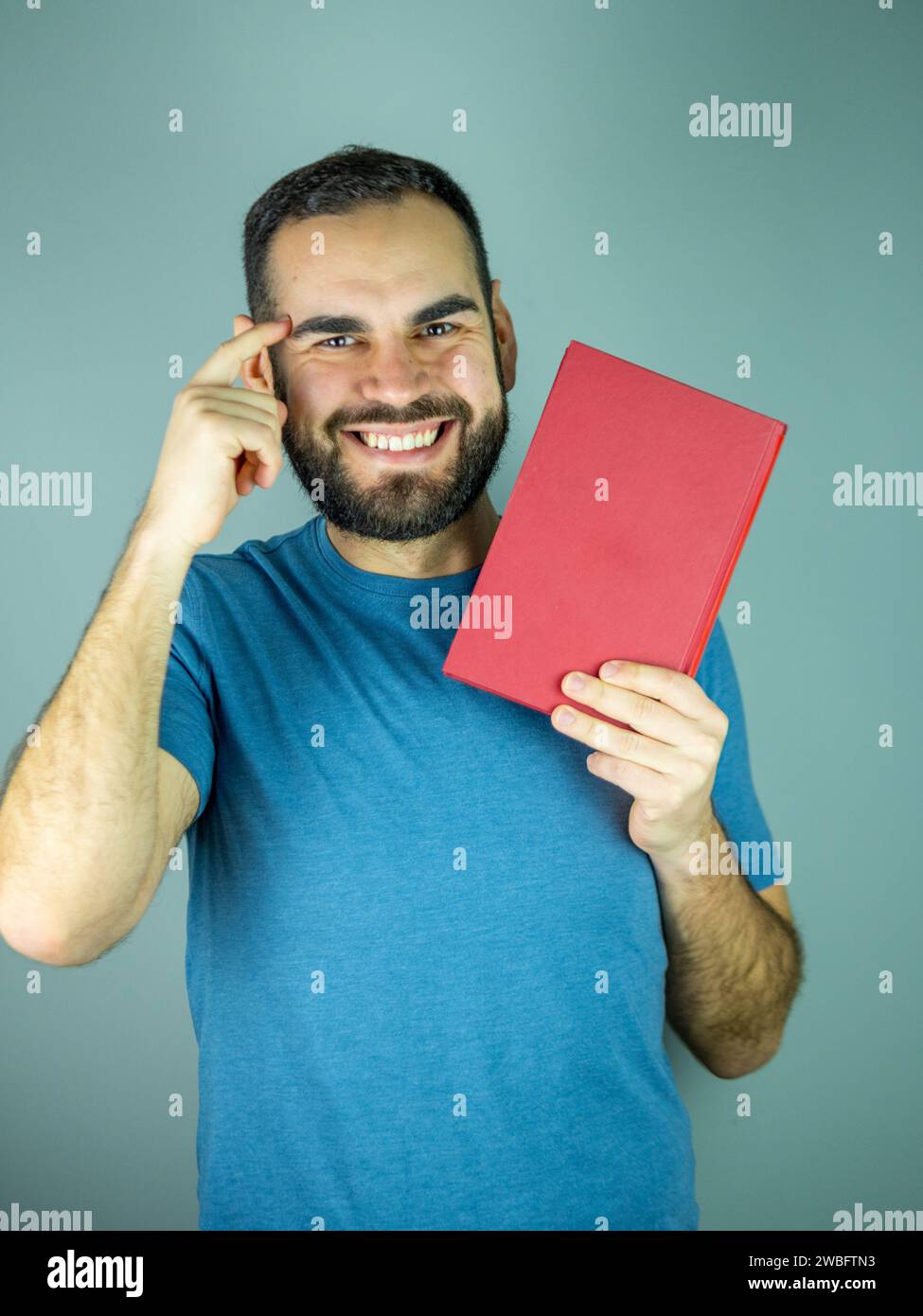 Young man pointing his head while holding a red book Looking at camera ...