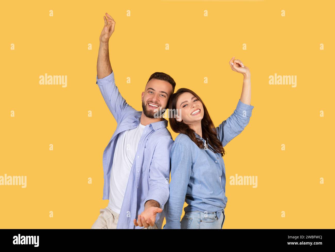 Excited couple with raised arms dancing on a joyful yellow background ...