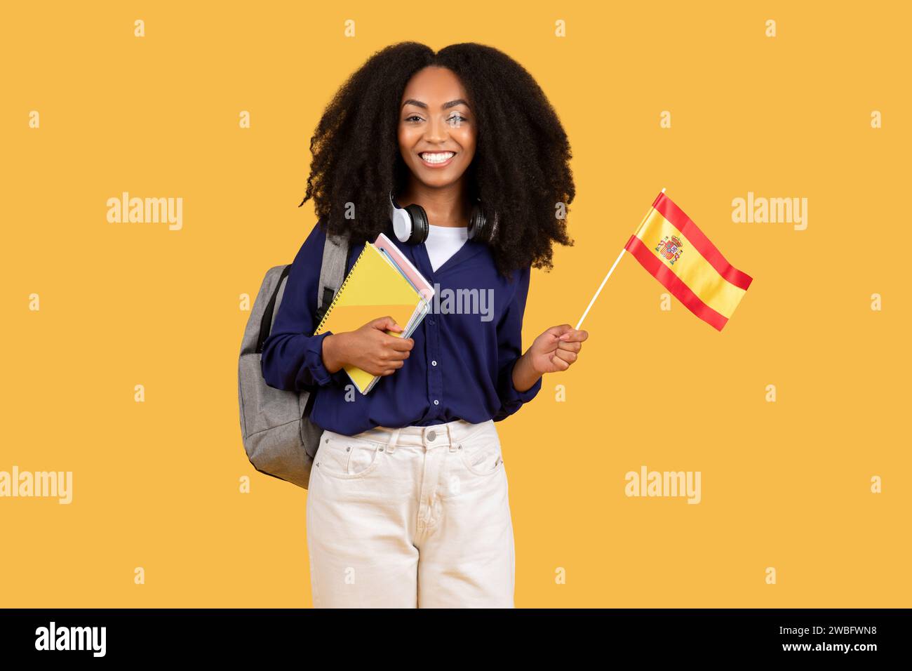 Happy black female student with backpack and copybooks, holding Spanish ...
