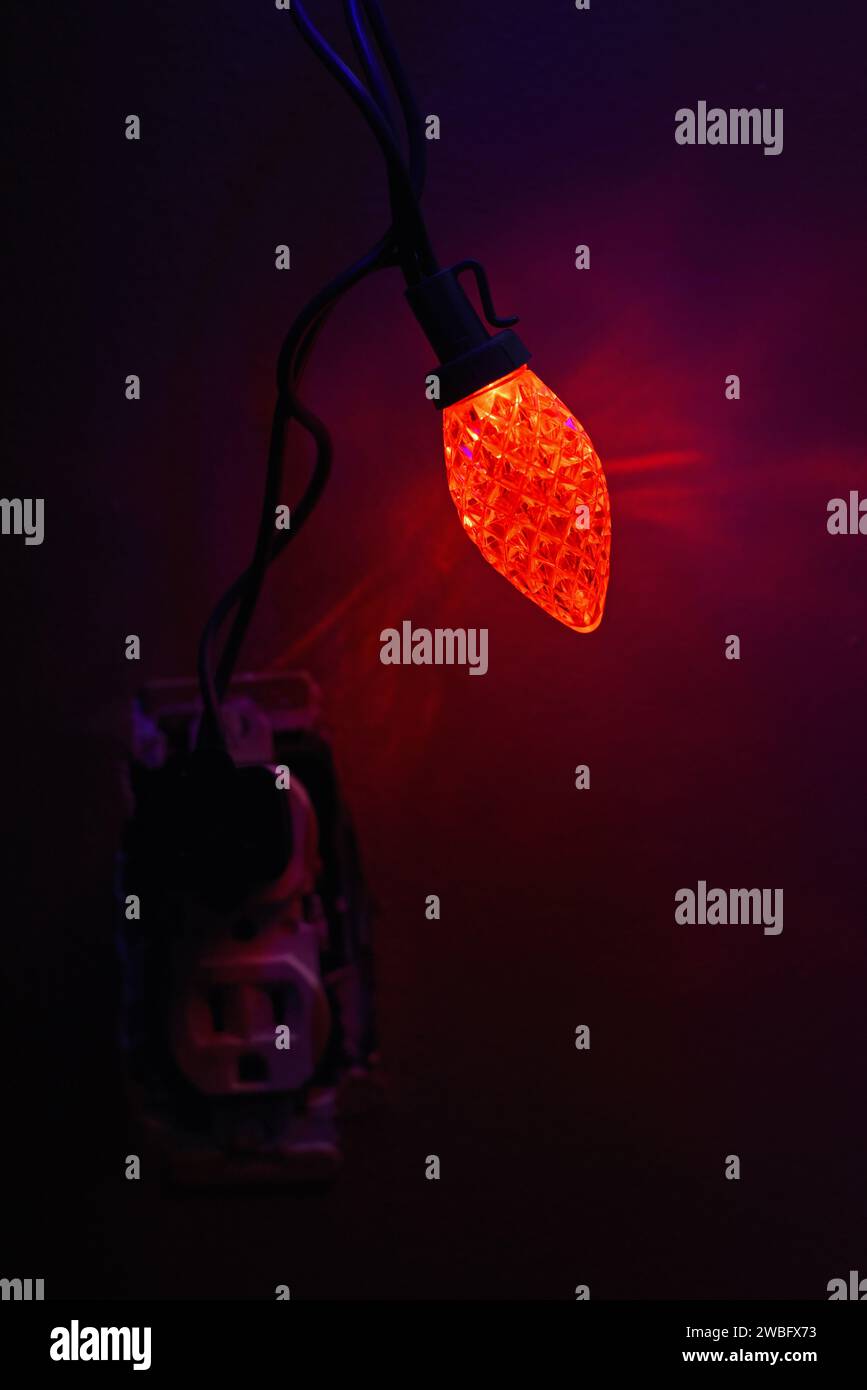 A red Christmas light hangs above an electrical plug in Stock Photo - Alamy
