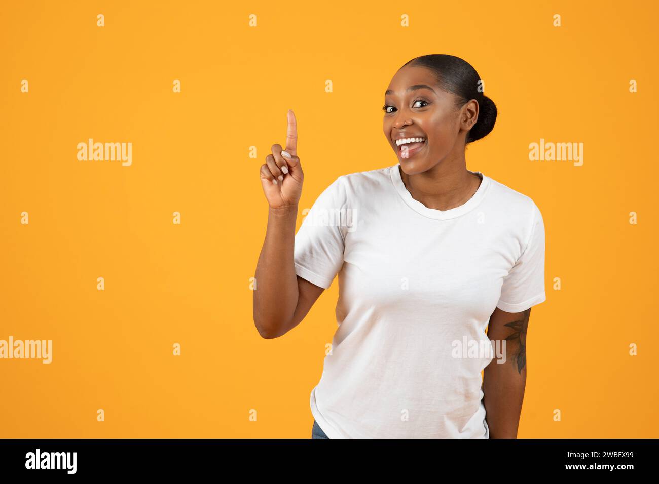 Happy black lady pointing finger upwards on yellow studio background ...
