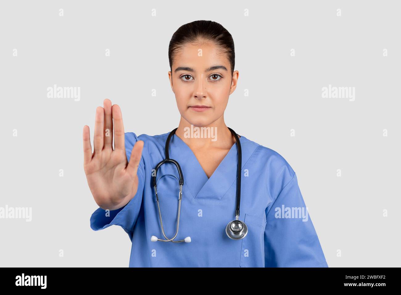 Determined european nurse in blue scrubs making a stop sign with her ...